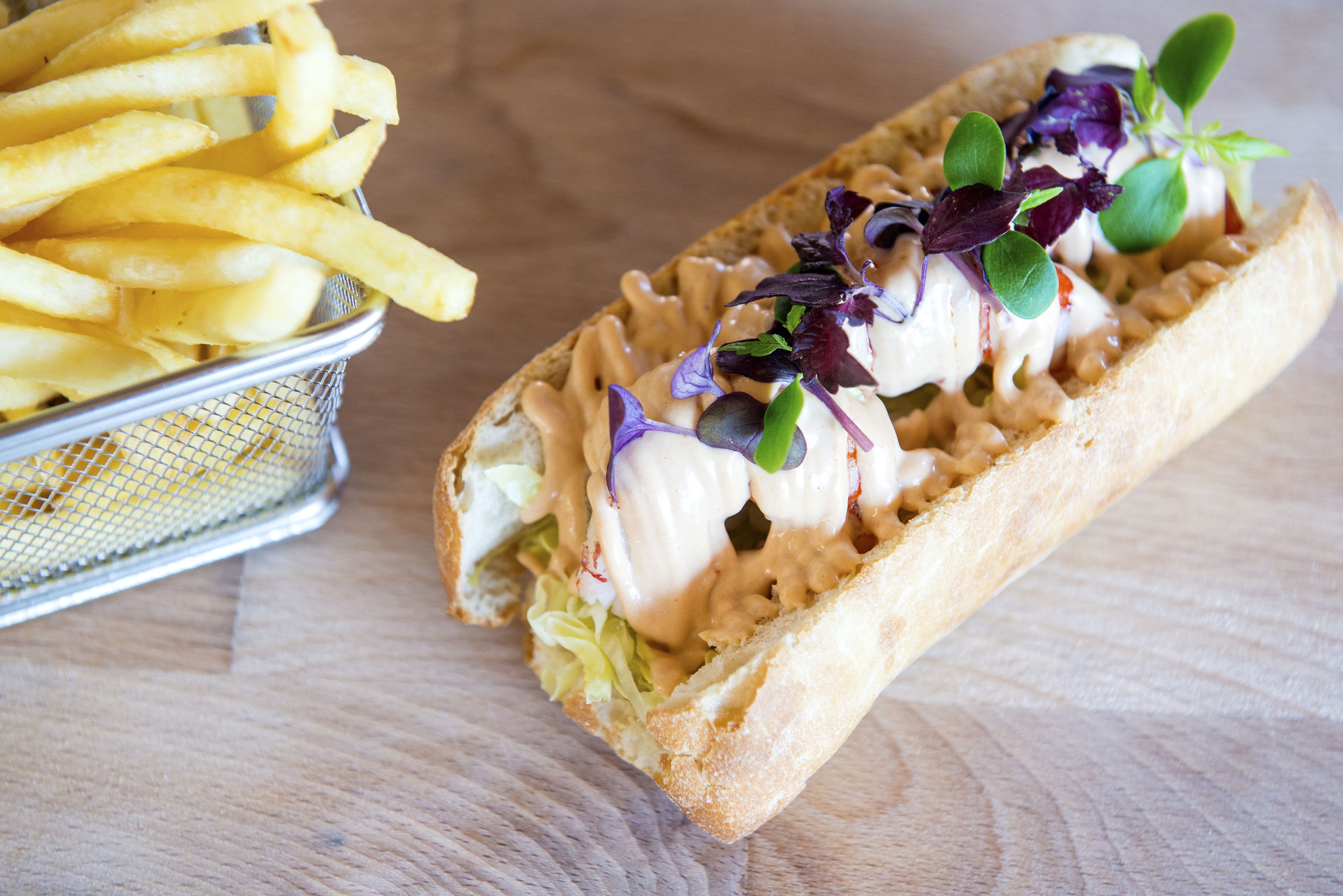 Um sanduíche com alface, molho e vegetais numa baguete, e um cesto de batatas fritas.