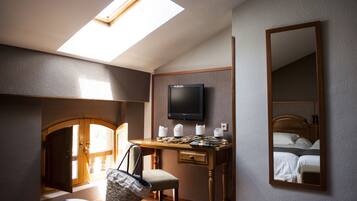 Quarto de hotel com claraboia, uma escrivaninha com televisão, um espelho grande e uma cama.