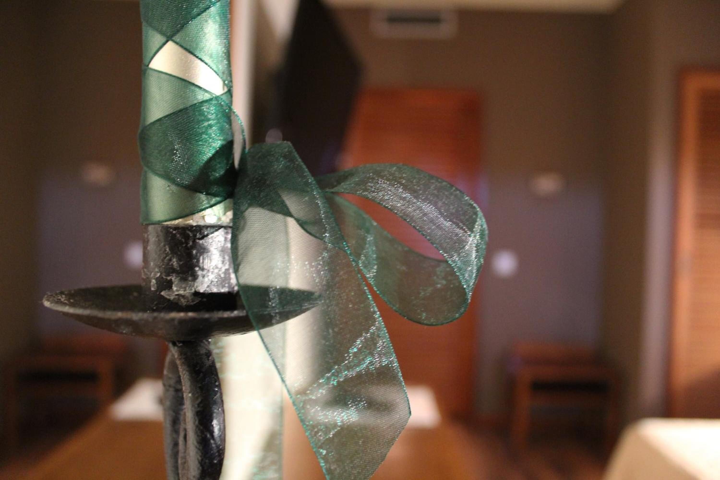 Um close-up de uma fita verde amarrada em um poste de metal, provavelmente parte de um elemento decorativo.