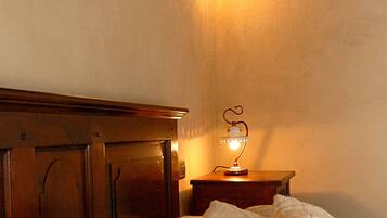 Quarto com cabeceira de madeira, mesa de cabeceira com abajur e colcha branca com textura.