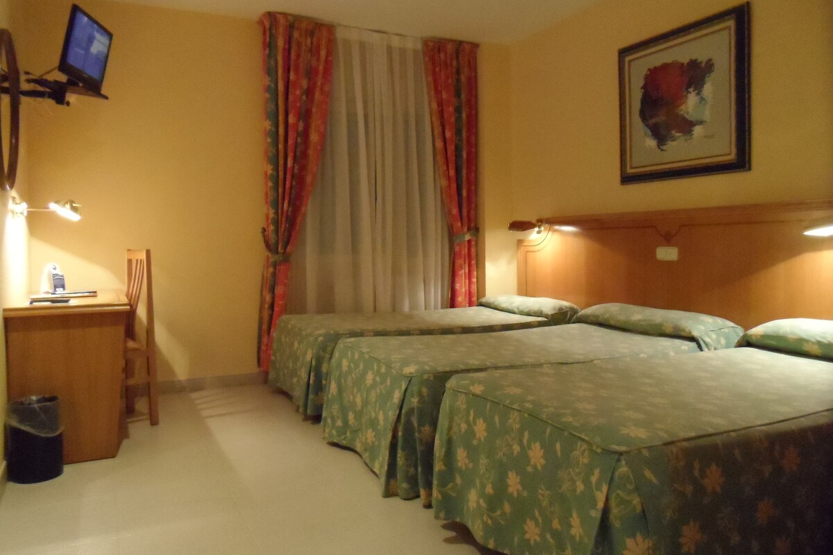 Quarto de hotel com duas camas, uma escrivaninha com computador, uma cadeira e um cesto de lixo.