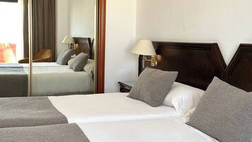 Quarto de hotel com uma cama grande, mesa de cabeceira com abajur, espelho e vista para o exterior.