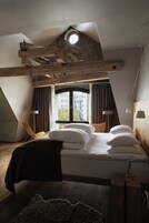 Quarto moderno no estilo loft, com teto inclinado, uma cama grande e vista para edifícios através de uma janela.