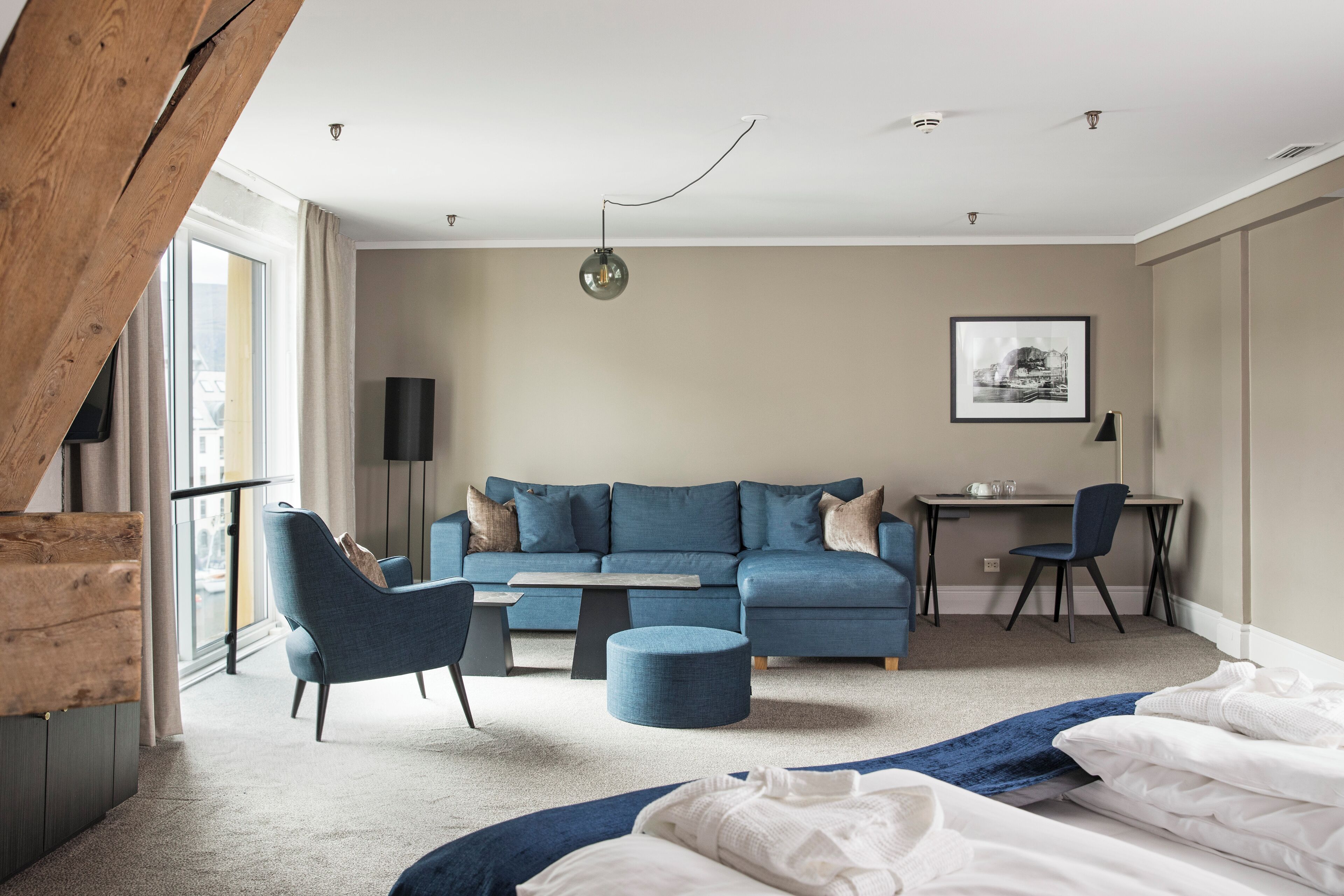 Quarto de hotel moderno com sofá seccional, escrivaninha, cadeira e cama.