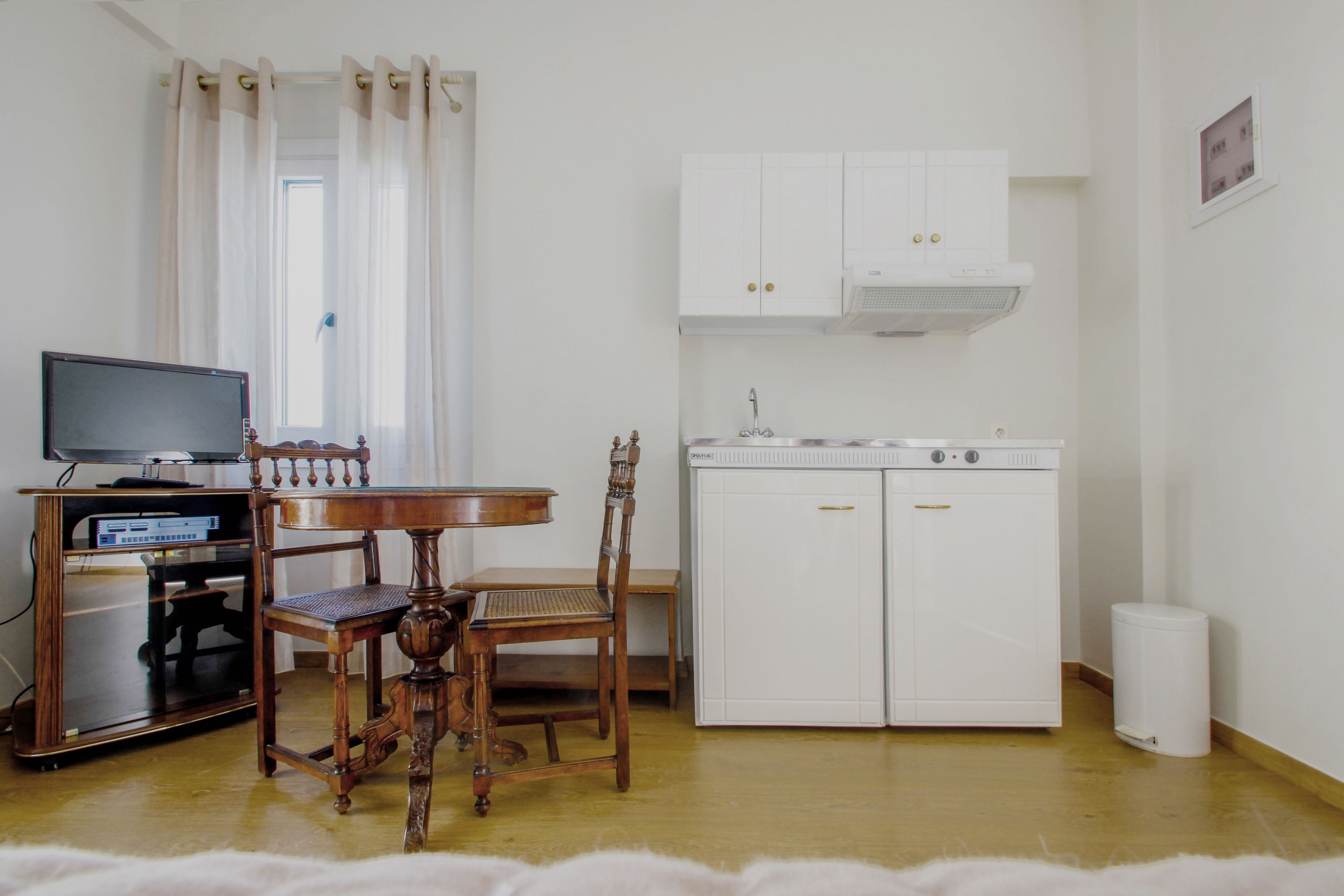 Uma cozinha compacta com uma mesa de jantar e cadeiras, uma televisão e uma geladeira branca.