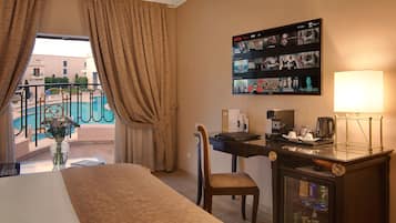 Quarto de hotel com cama, escrivaninha com luminária, cadeira, TV exibindo Netflix e vista para uma piscina.