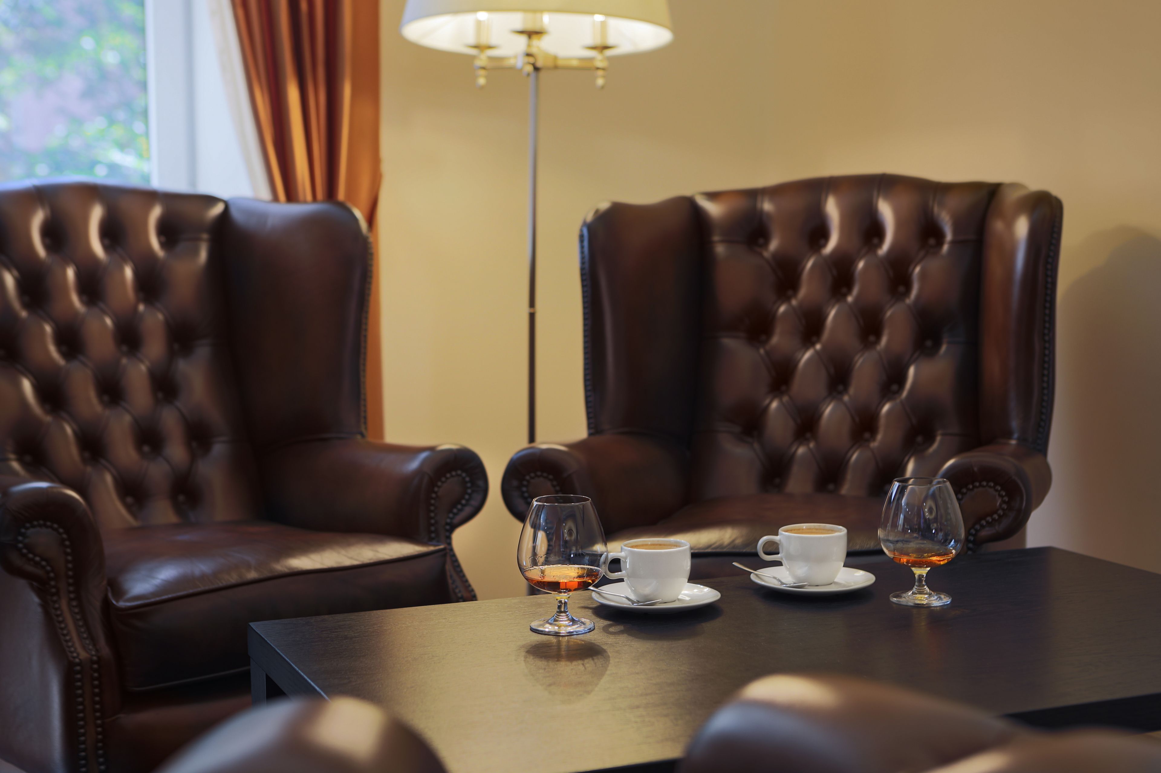 Quarto com duas poltronas de couro e uma mesa com uma xícara de café e um copo de uísque.