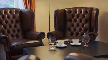 Quarto com duas poltronas de couro e uma mesa com uma xícara de café e um copo de uísque.