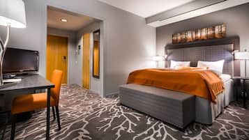 Quarto de hotel com cama, escrivaninha, cadeira, televisão e abajur.