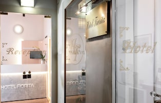 Uma área de recepção com porta de vidro, balcão de recepção e placa com a inscrição 'Hotel Fiorita'.