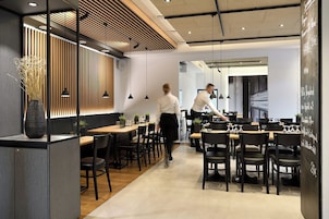 Interior moderno de restaurante com painéis de madeira, cadeiras pretas e um quadro negro com o menu.