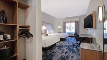 Quarto de hotel com duas camas, uma escrivaninha, uma cadeira, televisão, guarda-roupa e banheiro.