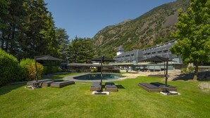 Área da piscina com espreguiçadeiras e guarda-sóis, rodeada por um gramado bem cuidado e um edifício com design moderno.