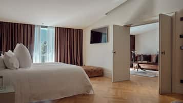 Quarto moderno com cama grande, TV fixada na parede e vista para uma sala de estar através de uma porta aberta.