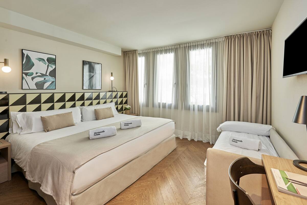 Quarto de hotel com cama, escrivaninha, cadeira e televisão.