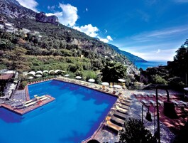 Piscina com espreguiçadeiras e guarda-sóis, cercada por vegetação exuberante e um cenário montanhoso.