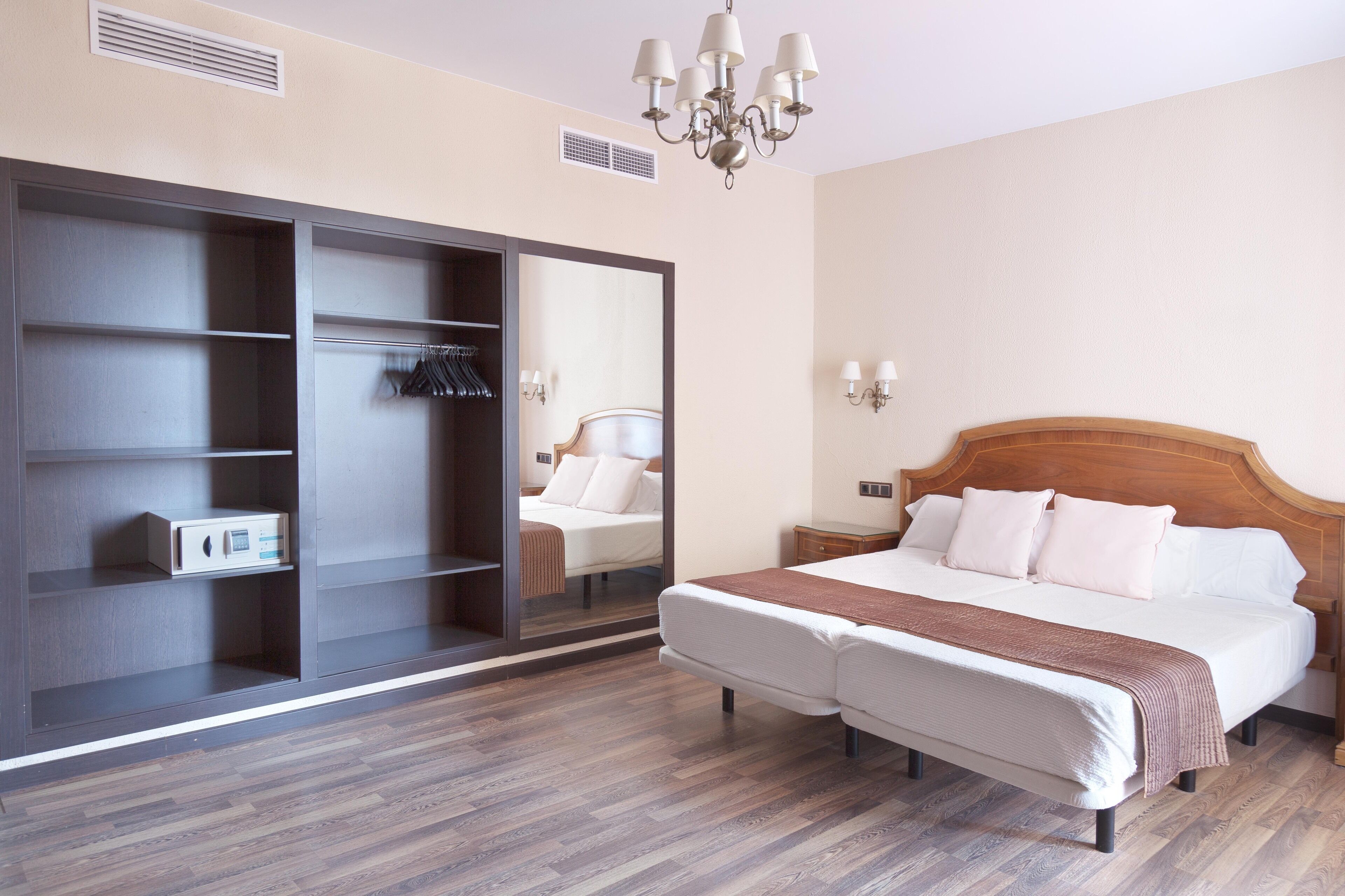 Quarto de hotel com um guarda-roupa grande, uma cama com roupa de cama branca, cabeceira de madeira e um candelabro.