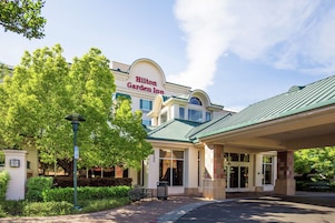 Um Hilton Garden Inn com telhado verde, entrada coberta e céu claro.