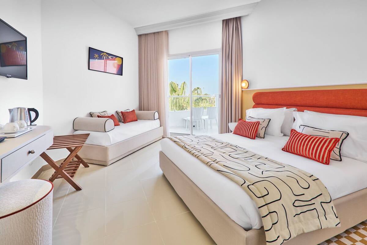 Quarto de hotel moderno com uma cama grande, um sofá, uma escrivaninha com cadeira e varanda com vista.