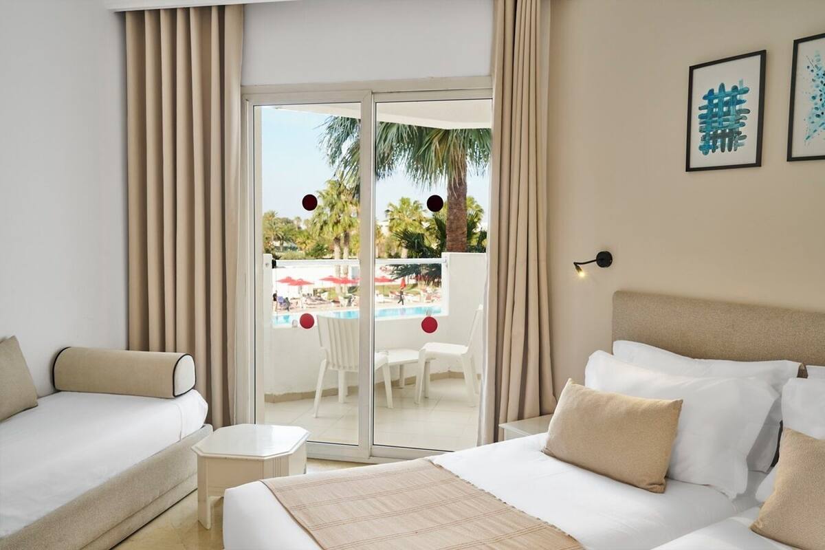 Quarto de hotel com cama, uma mesa pequena, varanda com vista para a piscina e porta deslizante.