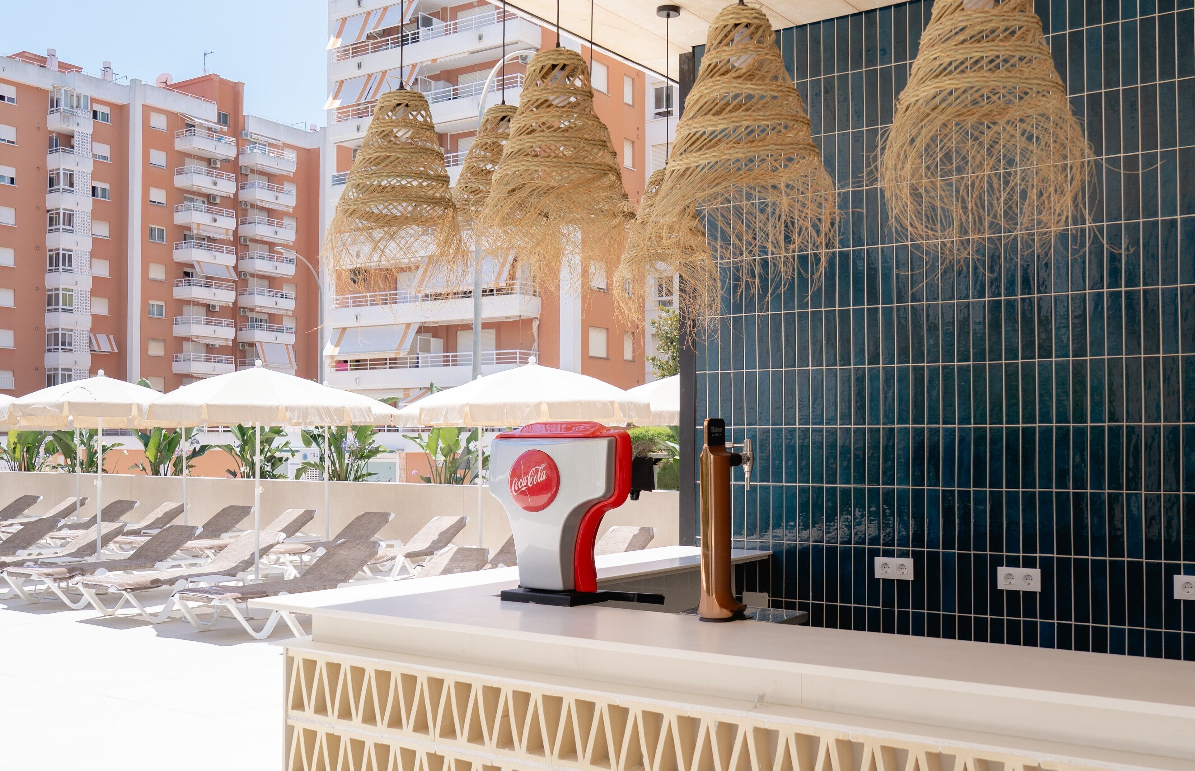 Uma área de piscina no terraço, com espreguiçadeiras, guarda-sóis e uma máquina de venda automática da Coca-Cola.