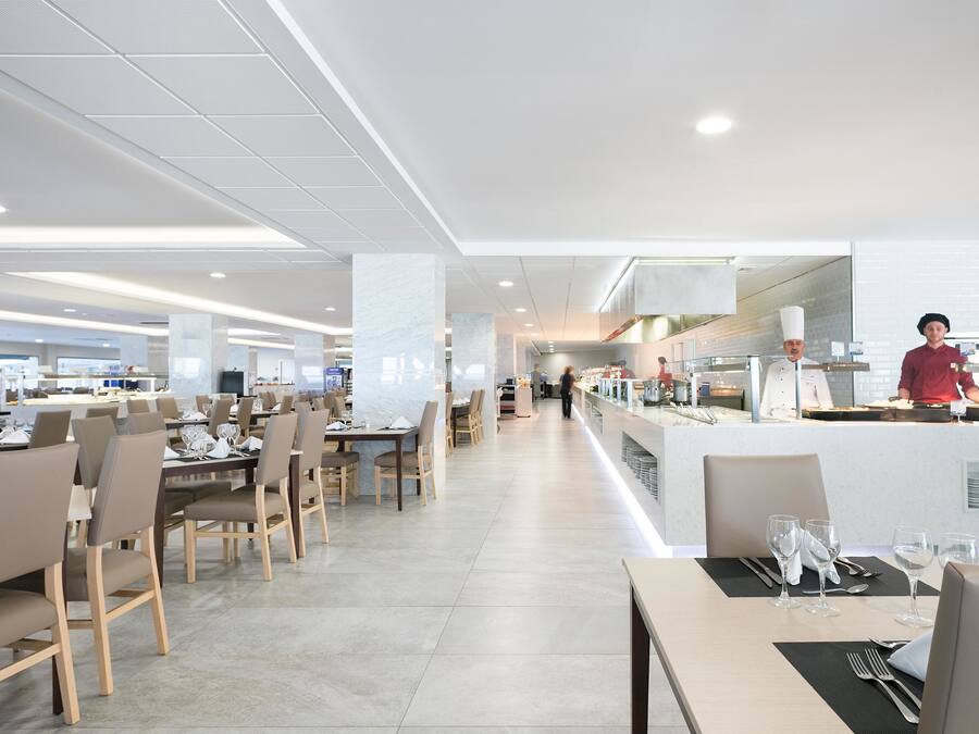 Um restaurante moderno com um balcão comprido, várias mesas e uma área de cozinha à vista.