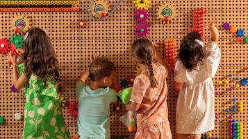 Crianças brincando com brinquedos em um painel perfurado.