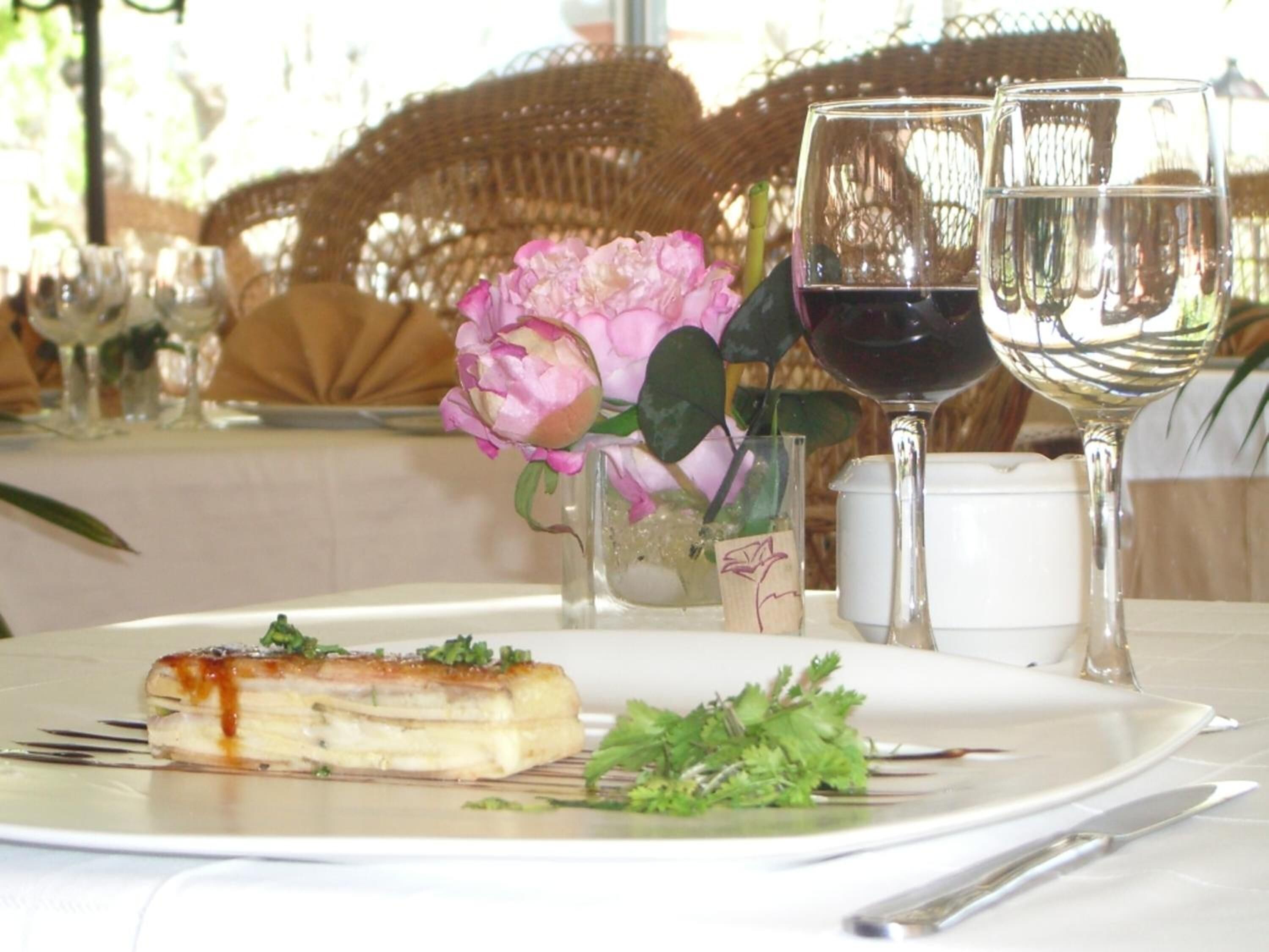 Uma mesa de jantar com um prato de comida, um copo de vinho tinto e um vaso com flores.