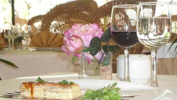 Uma mesa de jantar com um prato de comida, um copo de vinho tinto e um vaso com flores.