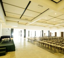 Um salão amplo com fileiras de cadeiras, palco com piano e alto teto com iluminação embutida.