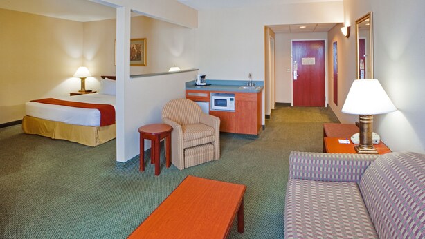 Quarto de hotel com cama, sofá, mesinha, cozinha compacta e espelho.