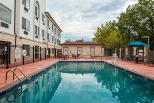 Piscina com um edifício de pedra ao fundo, uma torre de salva-vidas e área de estar externa.