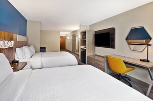 Quarto de hotel com duas camas, uma escrivaninha, uma cadeira, uma televisão e um espelho.