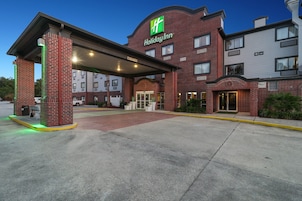 Um hotel Holiday Inn com fachada de tijolos, entrada coberta e estacionamento.