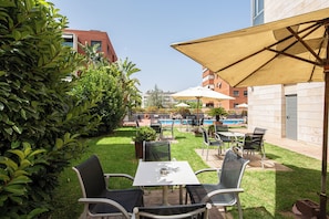 Uma área de pátio externa com mesas, cadeiras, piscina e vista para os edifícios ao redor.