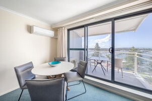 Quarto com mesa redonda, quatro cadeiras, uma tigela e uma janela grande com vista para a água e edifícios.