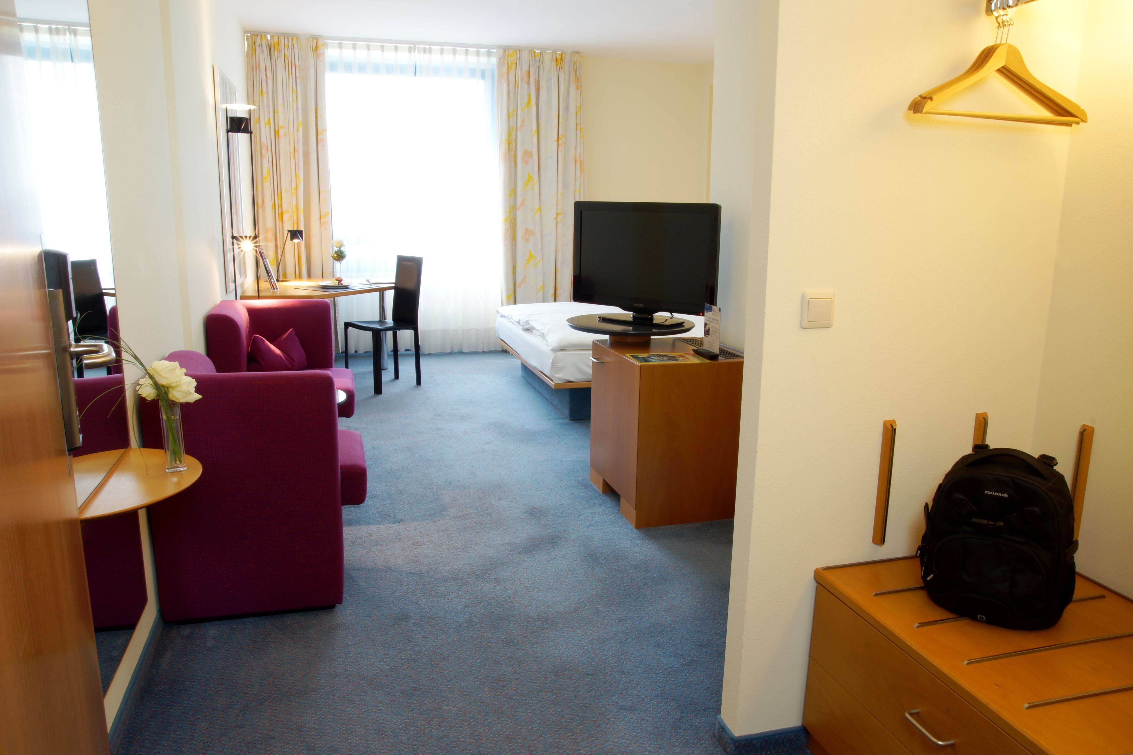 Quarto de hotel com cama, escrivaninha, cadeira, televisão e armário.