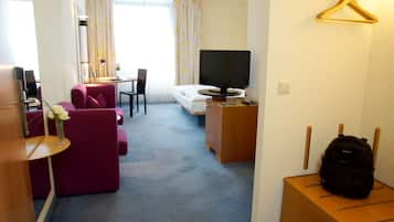 Quarto de hotel com cama, escrivaninha, cadeira, televisão e armário.
