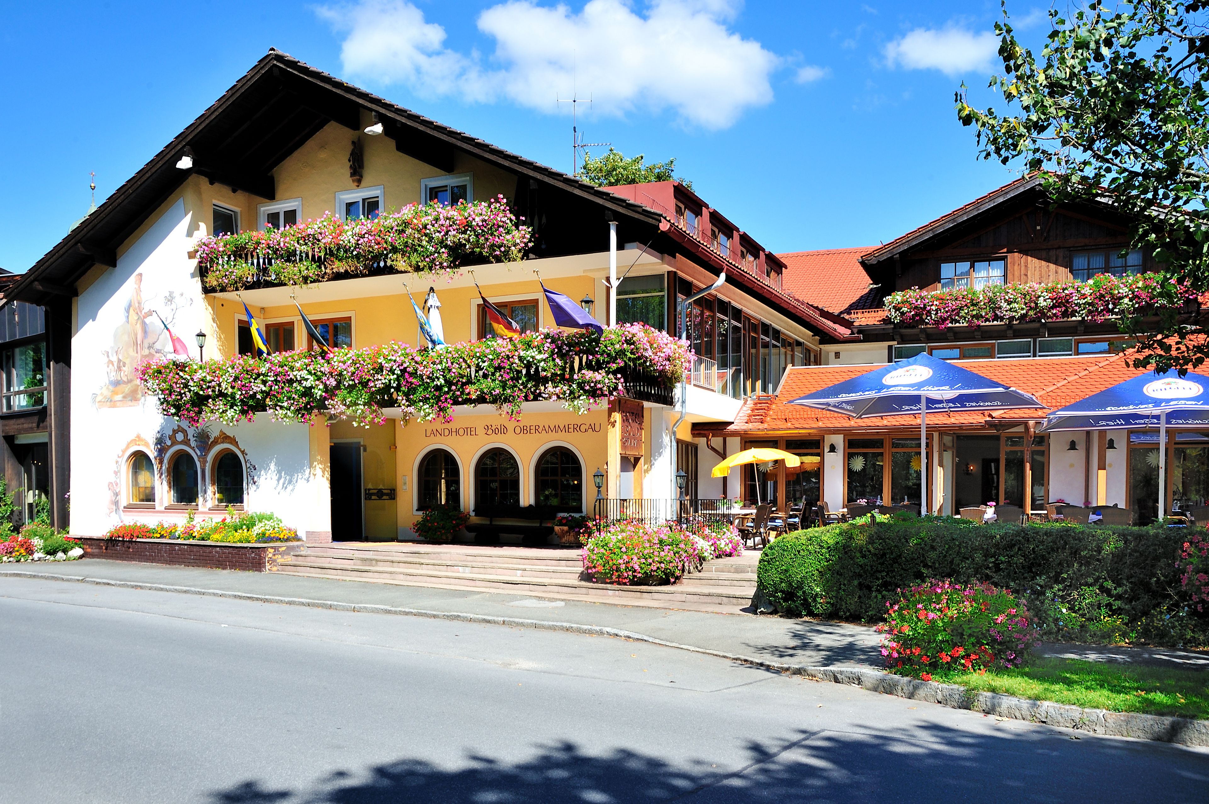 Um hotel com fachada amarela, varandas floridas e área de estar externa com guarda-sóis.