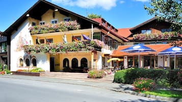 Um hotel com fachada amarela, varandas floridas e área de estar externa com guarda-sóis.