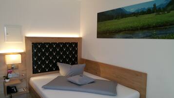 Um quarto com uma cama, uma mesa de cabeceira com uma luminária, uma pequena mesa com um vaso de flores e um quadro de uma paisagem na parede.