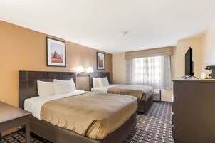 Quarto de hotel com duas camas, uma escrivaninha, televisão e janela com cortinas.
