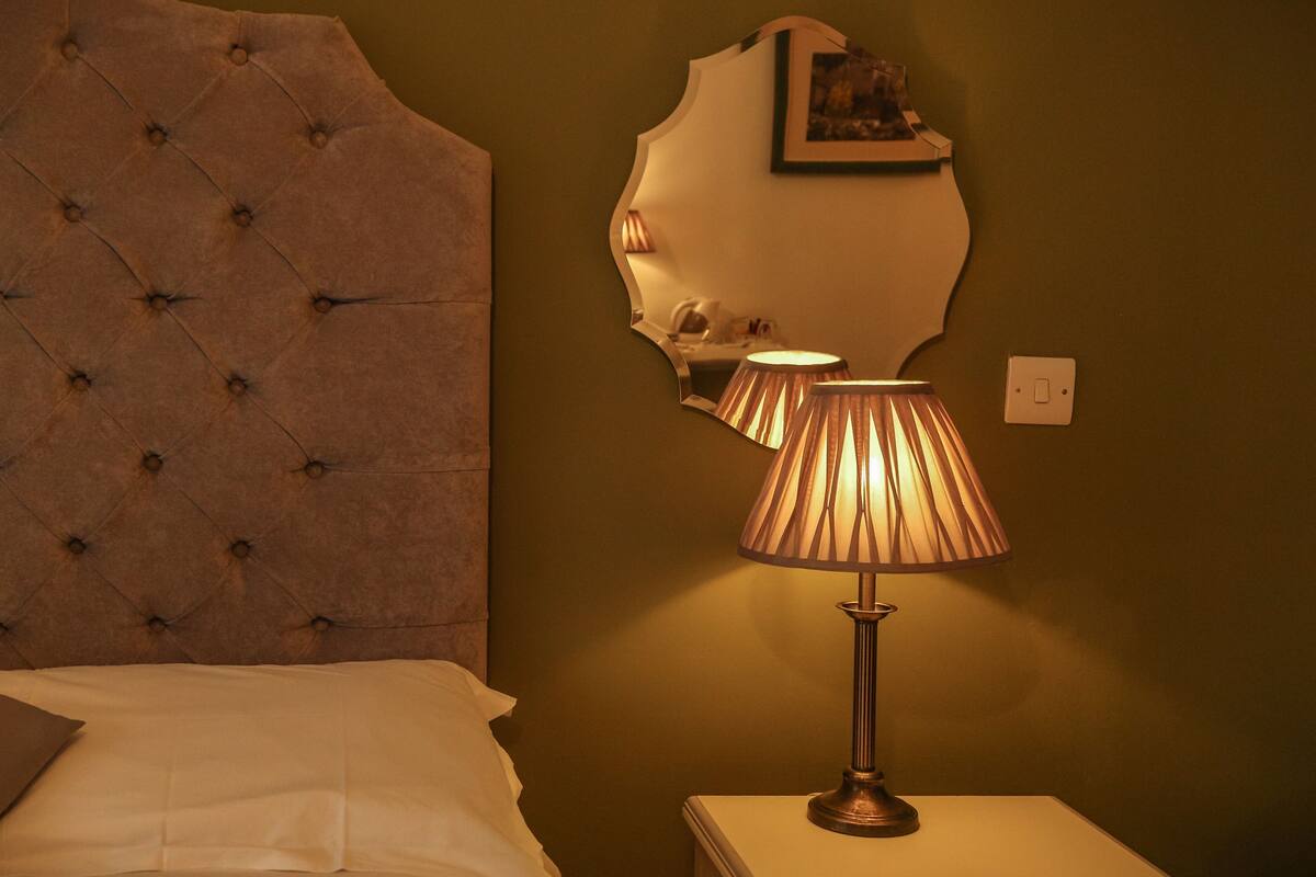 Quarto com cabeceira estofada, abajur, espelho e um quadro na parede.