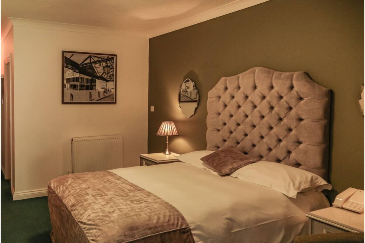 Quarto de hotel com uma cama grande, uma luminária de cabeceira, um radiador e um quadro na parede.