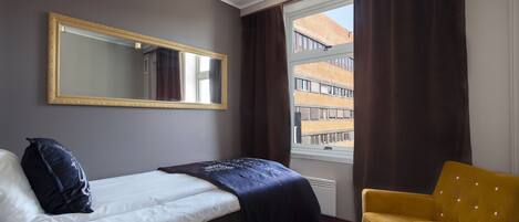 Quarto de hotel com cama, uma cadeira, um espelho grande e janela com cortinas.