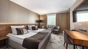 Quarto de hotel com uma cama grande, uma escrivaninha, uma cadeira, uma televisão e uma janela com cortinas.