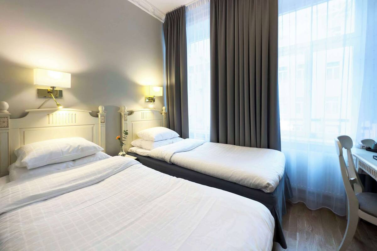 Quarto de hotel com duas camas, uma escrivaninha e uma cadeira.