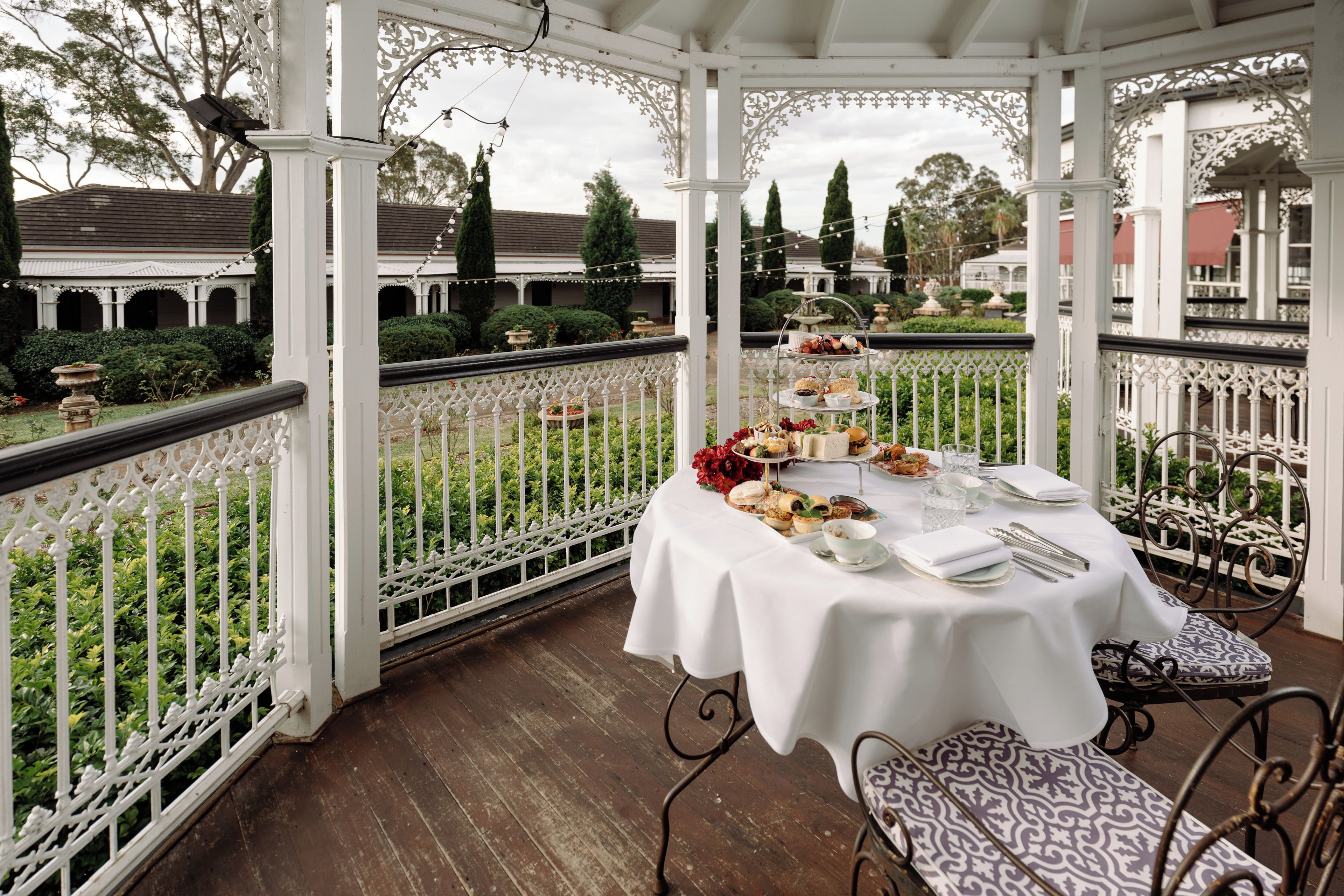 Área de refeições ao ar livre com mesa branca posta para uma refeição, cercada por um muro branco e vista para o jardim.