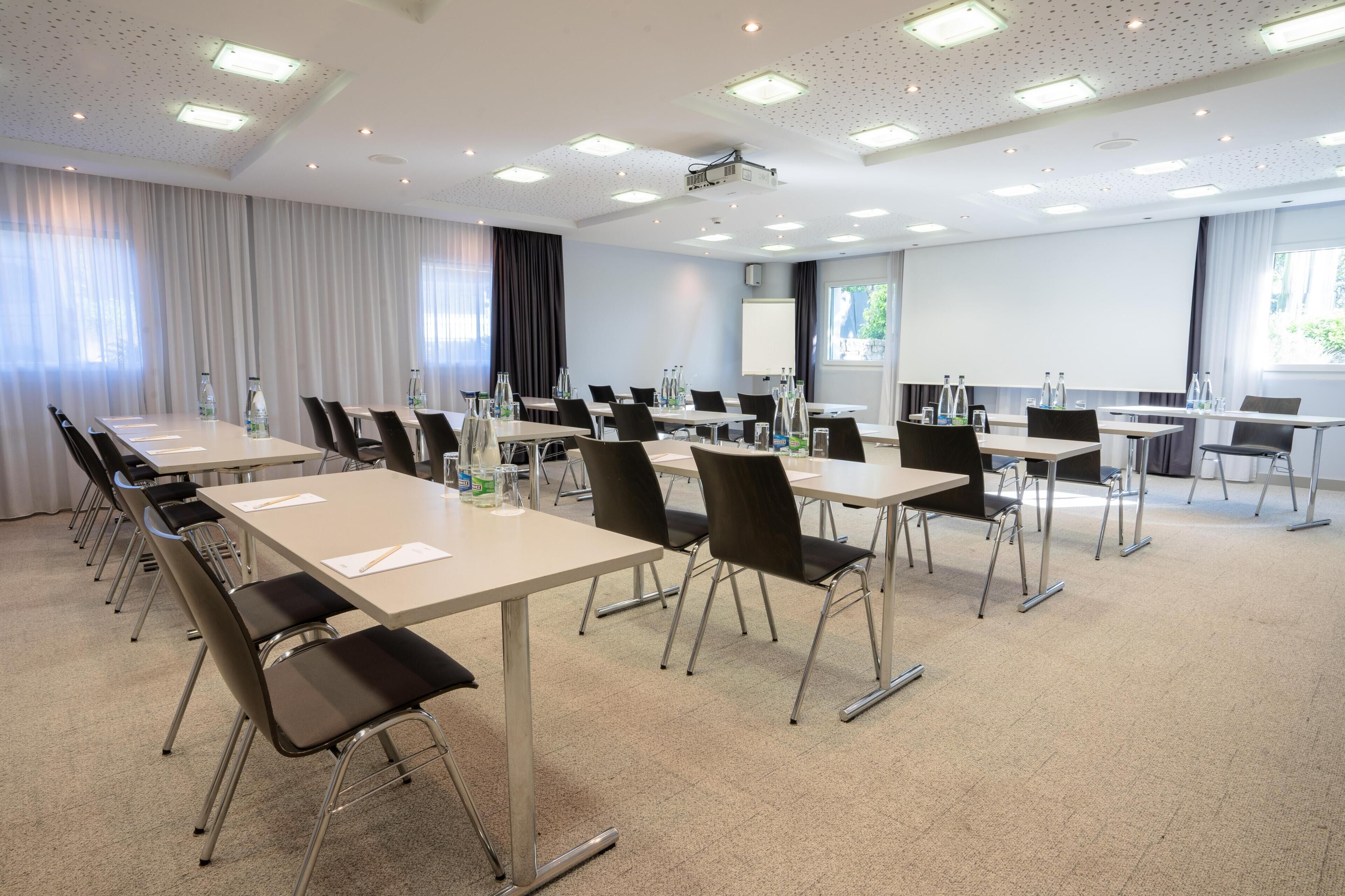 Uma sala de conferências com várias mesas, cadeiras, um projetor e um quadro branco.