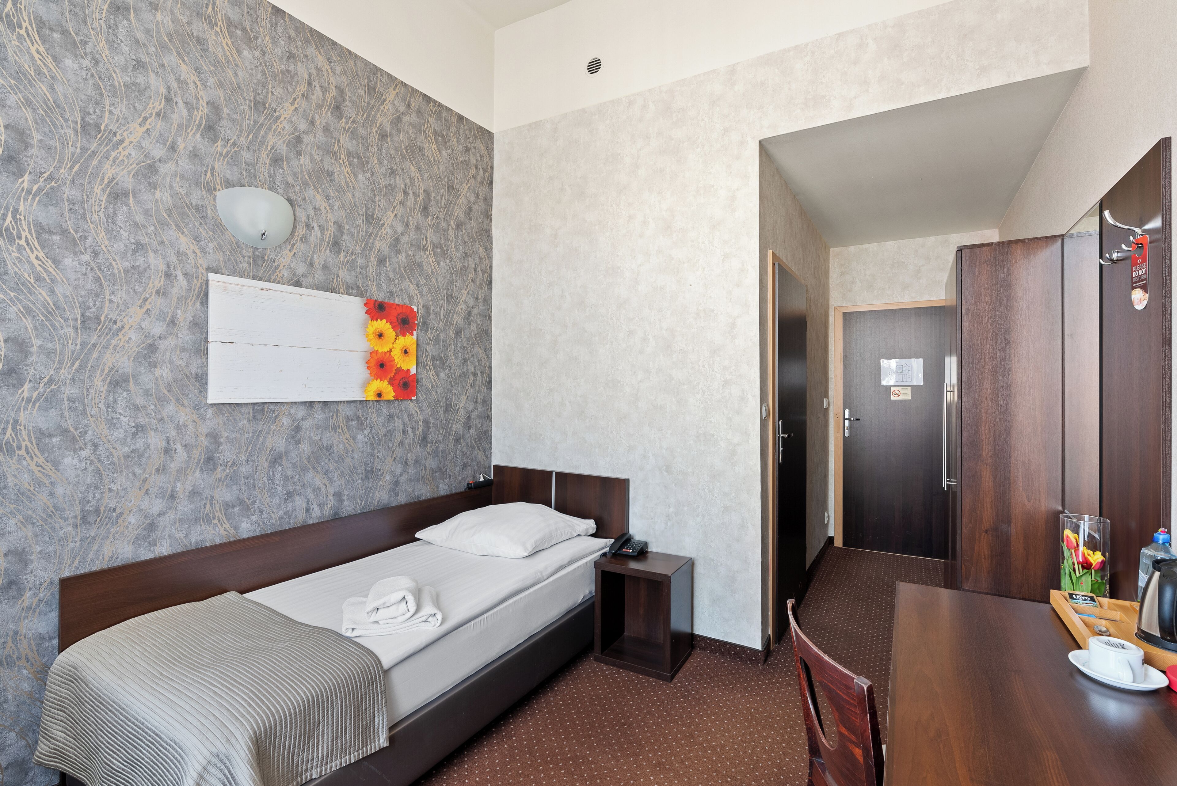 Quarto de hotel com cama, mesa de cabeceira e pequena escrivaninha com cadeira.